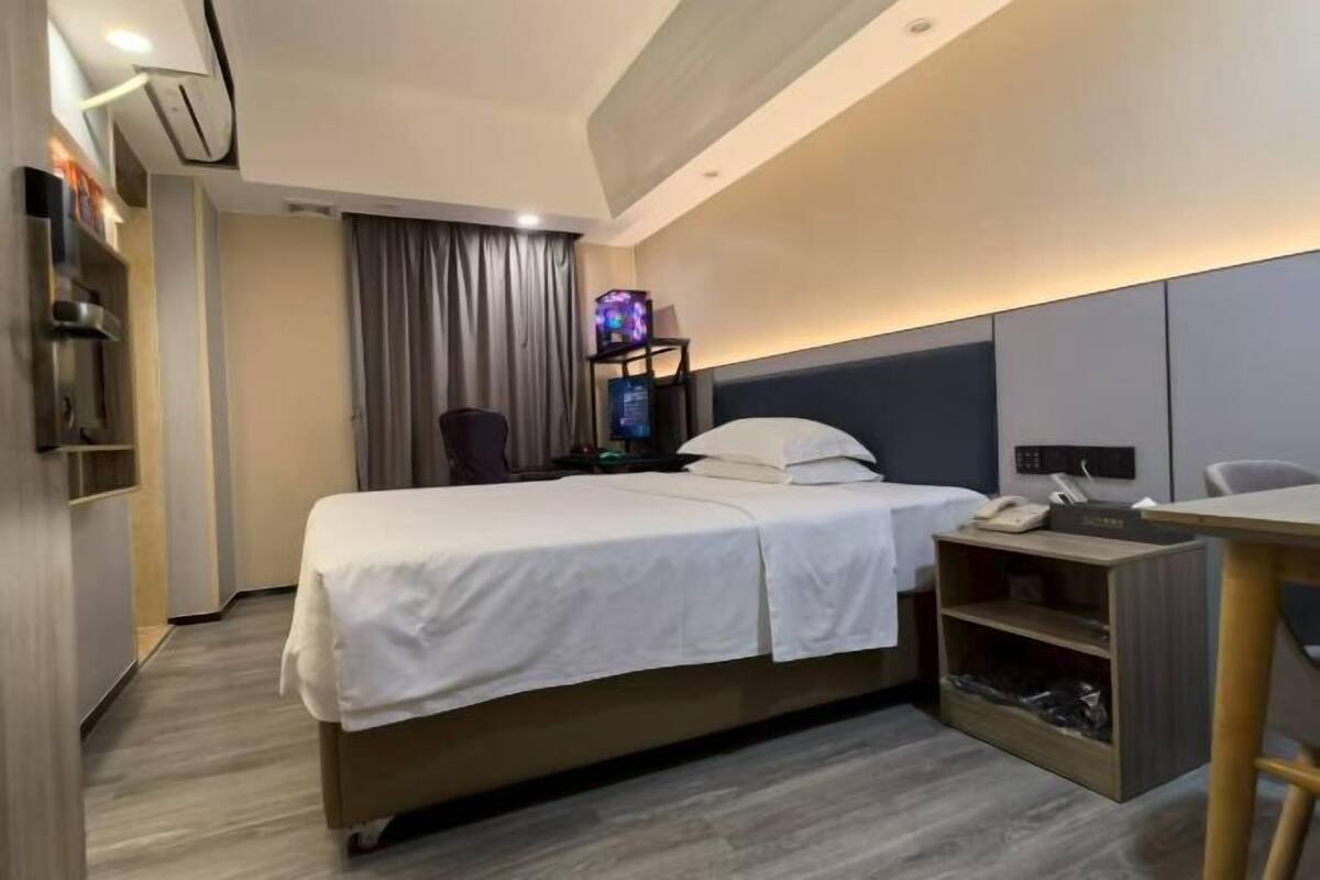Quarto de hotel com cama, escrivaninha, cadeira, televisão e minibar.