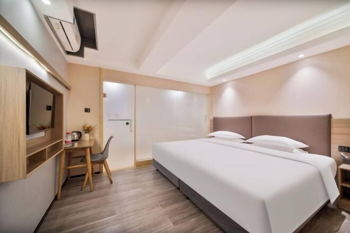 Quarto de hotel com cama, escrivaninha, cadeira, televisão e guarda-roupa.