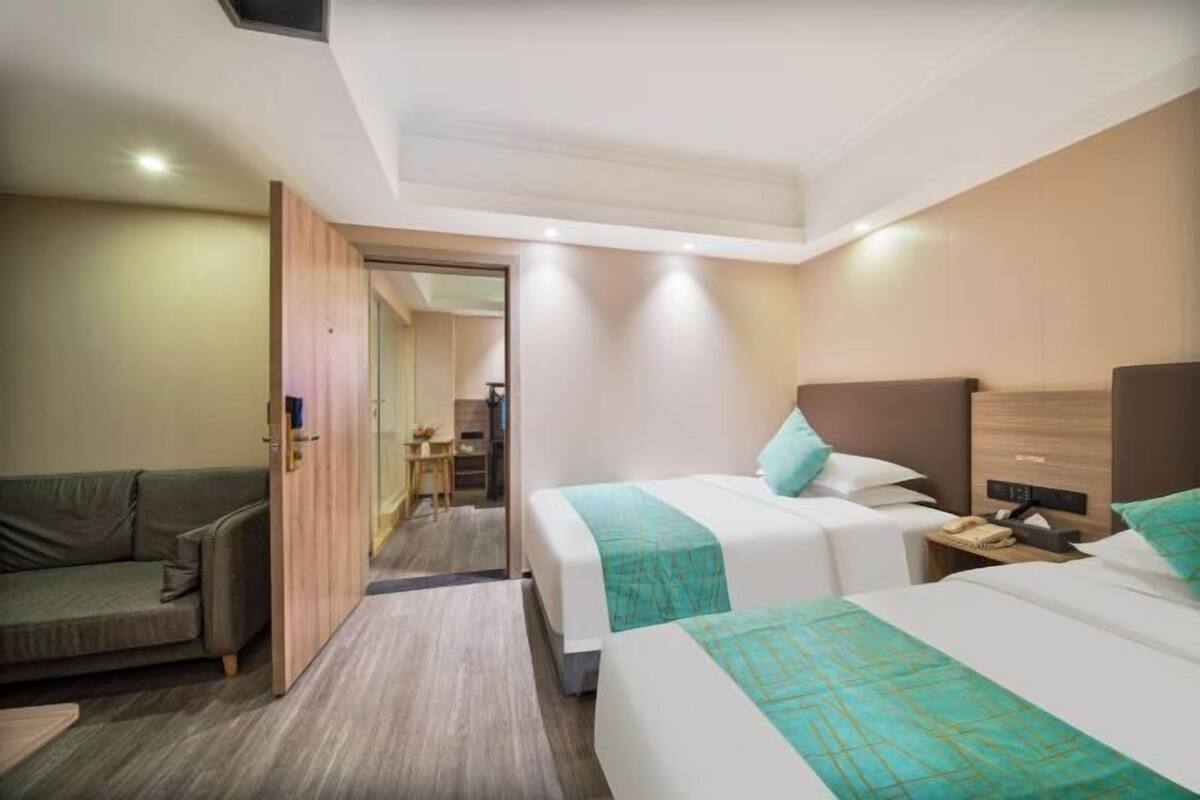 Quarto de hotel com duas camas, um sofá, uma escrivaninha e um banheiro visível por uma porta aberta.