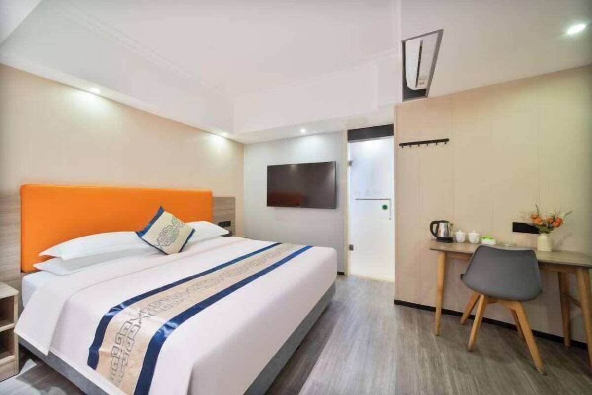 Quarto de hotel com cama, escrivaninha, cadeira, televisão e guarda-roupa.