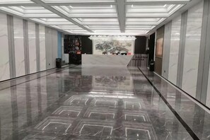 Um hall espaçoso com piso de mármore, balcão de recepção e uma obra de arte na parede.