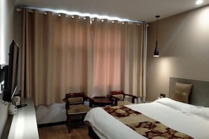 Quarto de hotel com uma cama, duas cadeiras, uma mesa pequena, uma televisão e cortinas.