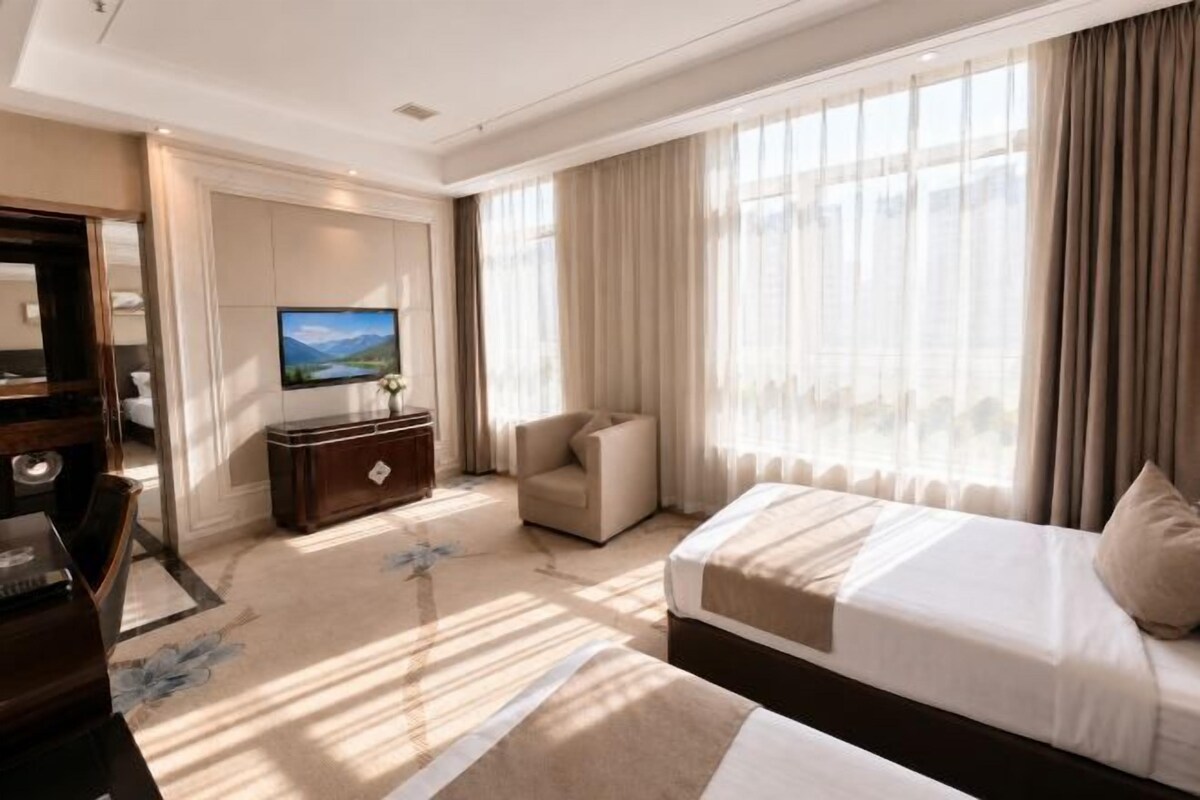 Quarto de hotel com cama, sofá, televisão e escrivaninha.