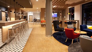 Uma área de bar moderna com um balcão comprido, vários bancos altos e um espaço de estar com sofás e cadeiras.