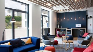 Um interior moderno com um sofá azul, cadeiras vermelhas e cinzentas, uma mesa de madeira redonda e uma escrivaninha com um computador.