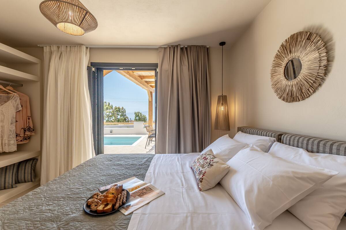 Quarto com cama, mesa lateral, revista, prato de comida e vista para piscina e área externa.