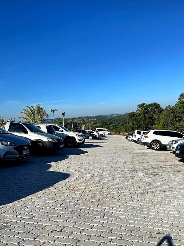 Estacionamento com vários carros, piso pavimentado e céu claro.
