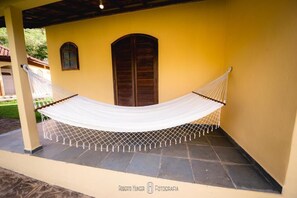 Uma rede montada entre duas portas de madeira numa parede amarela, com um chão em mosaicos e uma pequena janela acima das portas.