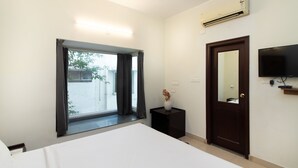 Quarto de hotel com uma cama grande, janela com cortinas, porta, TV fixada na parede e uma pequena mesa com um vaso.