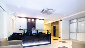 Uma área de recepção de hotel com design moderno, incluindo um balcão de atendimento, espaço para sentar e um recepcionista.