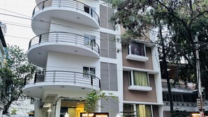 Um edifício residencial com várias andares, varandas, entrada com portão e um carro estacionado em frente.