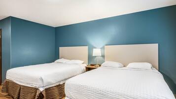 Quarto de hotel com duas camas de solteiro, mesa de cabeceira com luminária e piso de madeira.