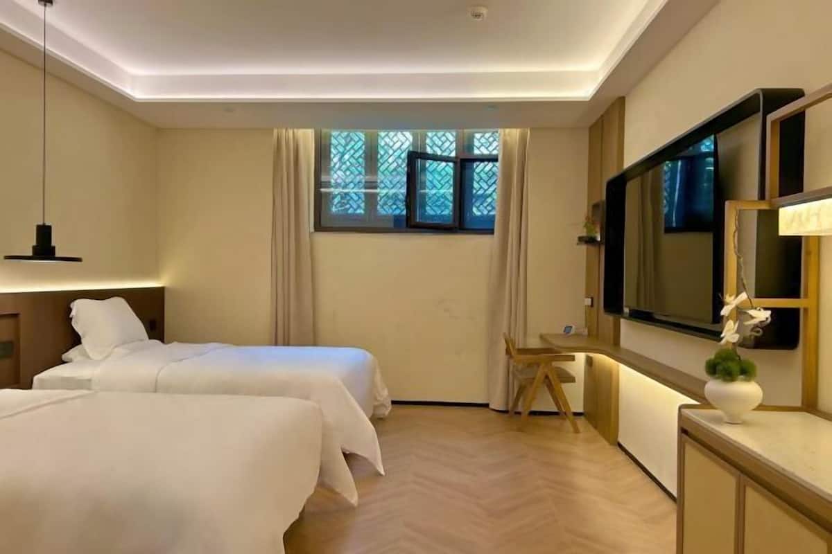 Quarto de hotel com duas camas, uma escrivaninha, uma televisão e uma janela com cortinas.