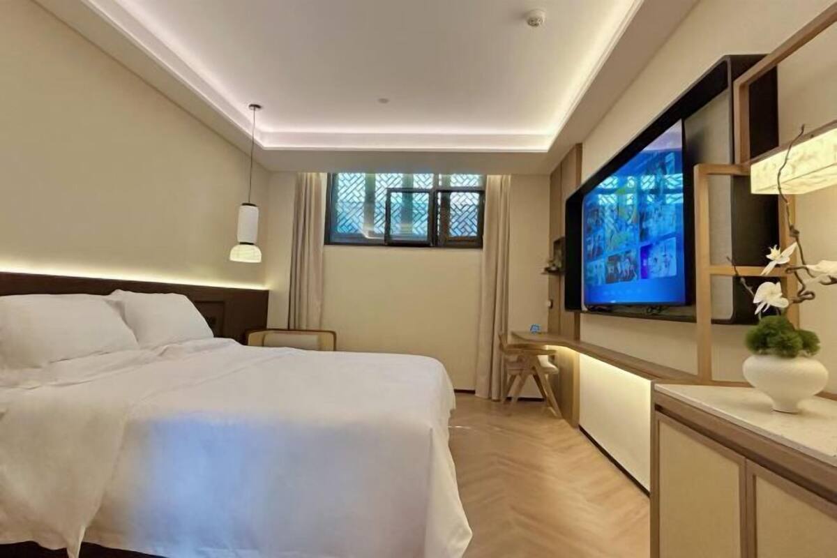 Quarto de hotel com cama grande, escrivaninha, televisão e janela com cortinas.