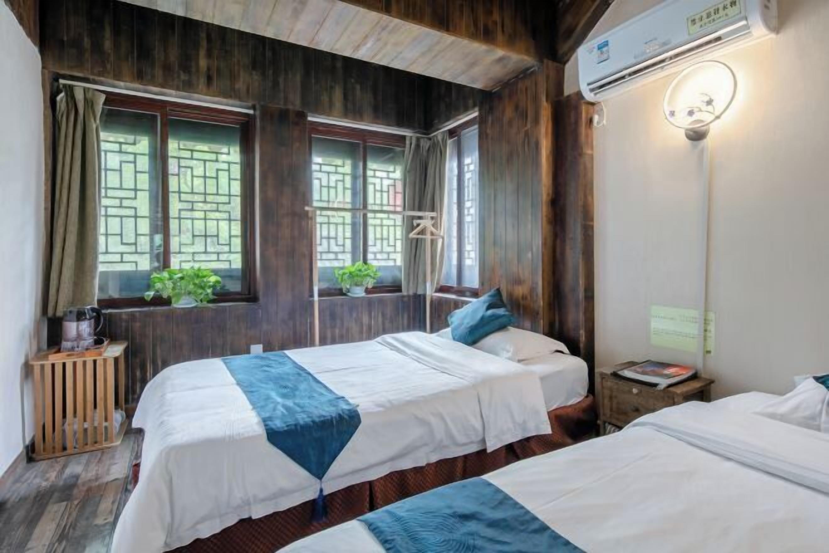 Quarto com duas camas, paredes de madeira, janela com vista e mesa de cabeceira com luminária.