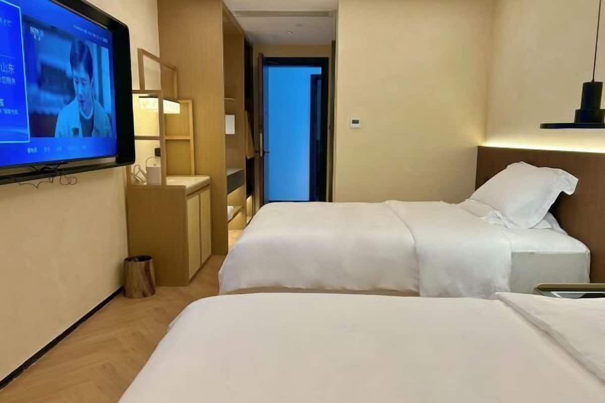 Quarto de hotel com duas camas, uma TV na parede e uma escrivaninha com uma cadeira.