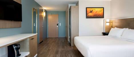 Quarto de hotel com cama, televisão, máquina de café e um quadro na parede.