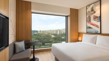 Quarto de hotel moderno com uma cama grande, um sofá, uma mesa pequena e uma televisão.