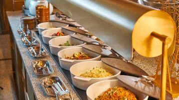 Uma mesa de buffet com diversos pratos, utensílios de servir e um carrinho dourado.