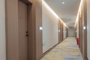 Corredor de hotel com portas, piso coberto por carpete e placas de saída de emergência.