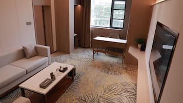 Quarto de hotel moderno com sofá, mesa de jantar, mesa de centro e televisão.