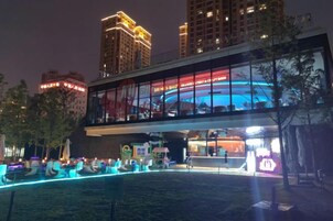 Um edifício moderno com fachada de vidro, um bar no terraço e uma entrada iluminada por neon.