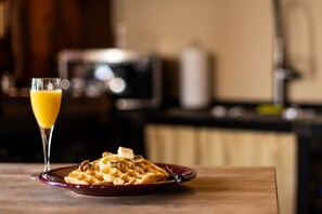 Uma pilha de waffles com um copo de suco de laranja sobre uma mesa de madeira.