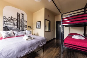 Quarto de hotel com uma cama, uma cama beliche, um mural na parede, um espelho e uma porta.