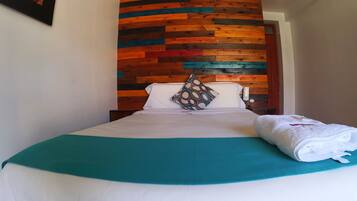 Uma cama bem arrumada com um cobre-leito verde-água e um travesseiro branco com padrão geométrico.
