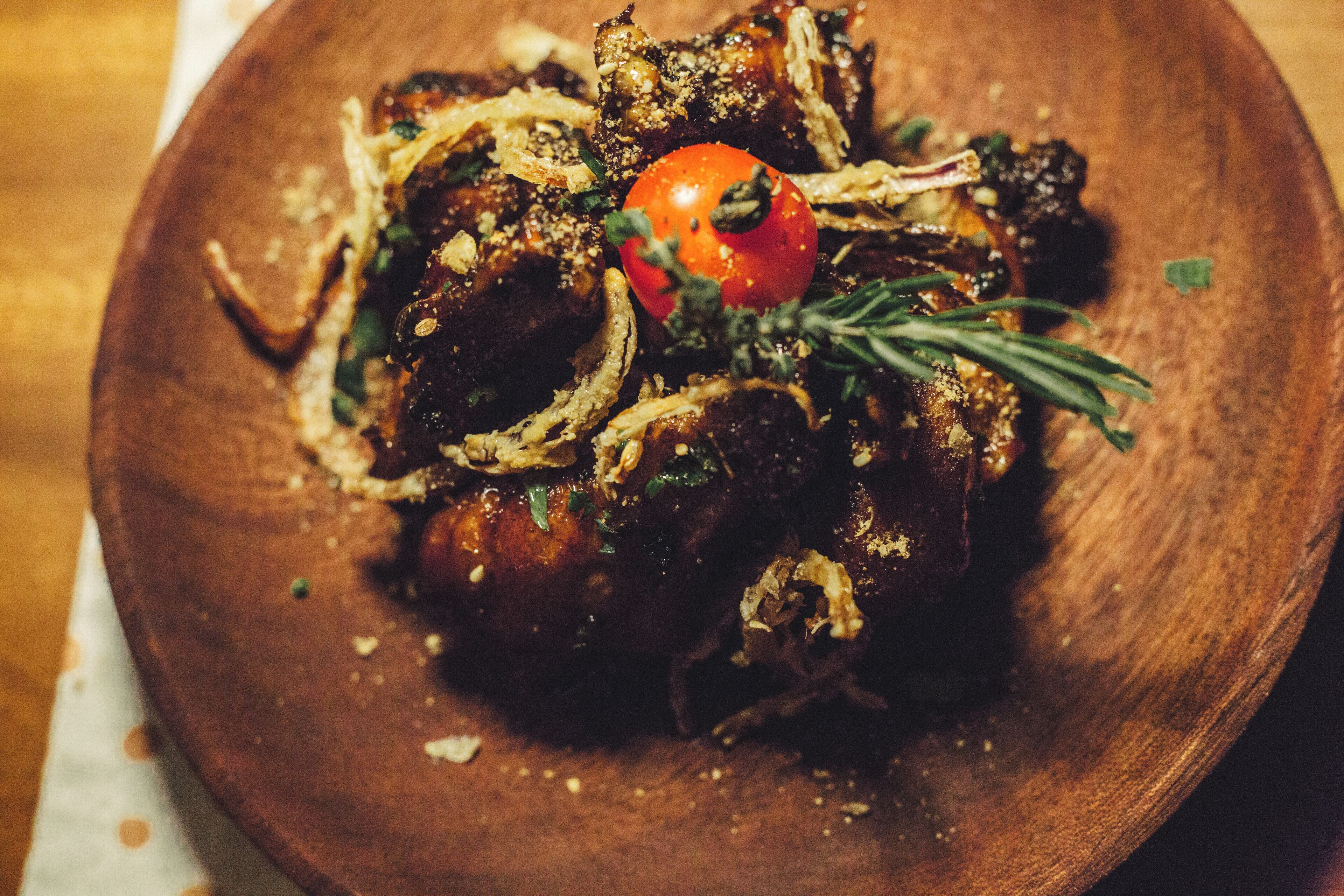 Um prato de madeira com carne, legumes e um tomate cereja, guarnecido com ervas.