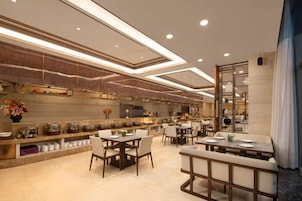 Um restaurante amplo com várias mesas e cadeiras, um balcão comprido com expositores de comida e um design de teto moderno.