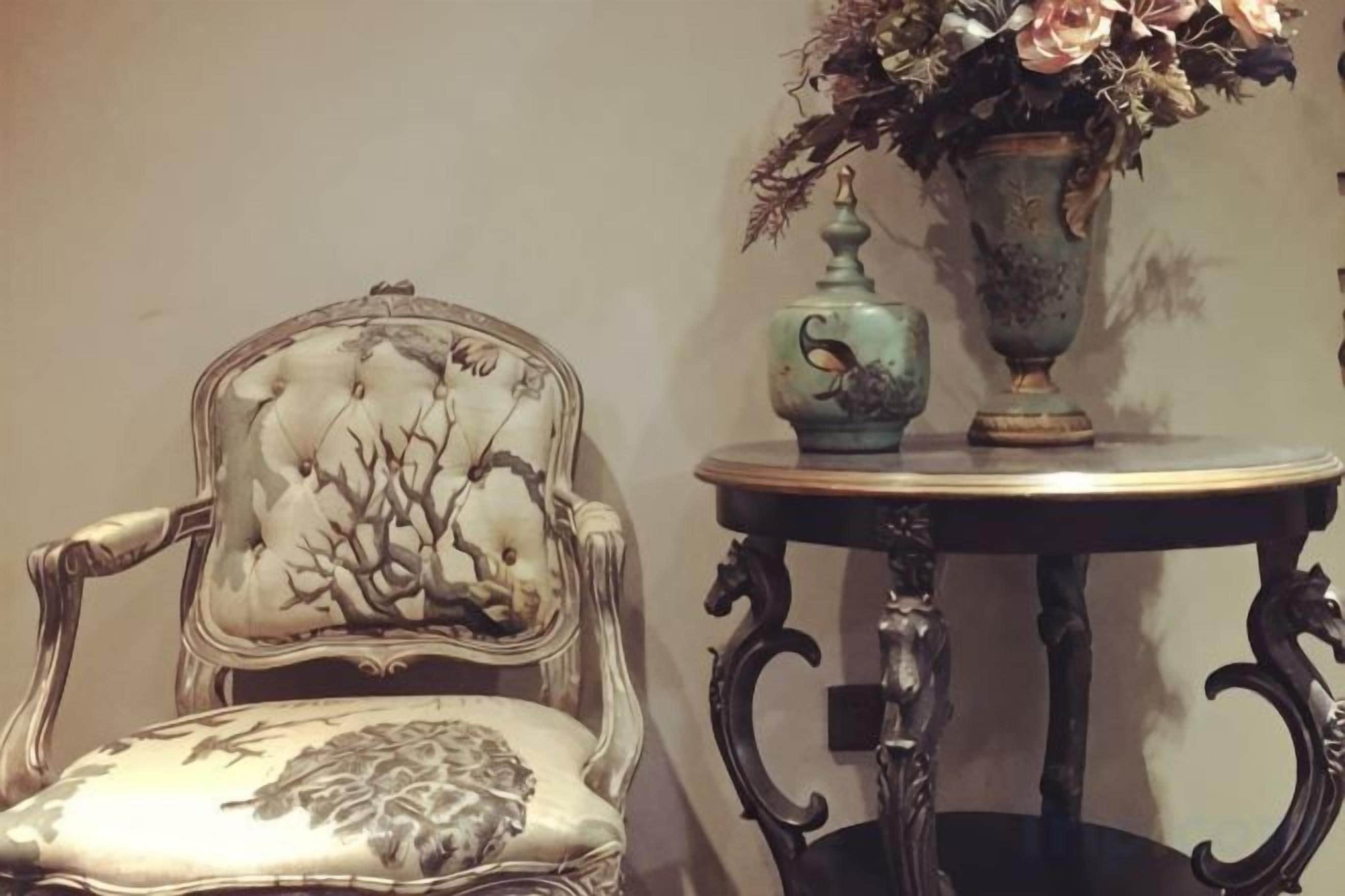 Uma cadeira antiga com padrão floral e uma mesa com um vaso.