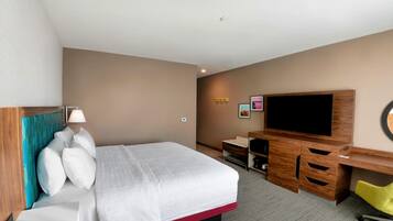 Quarto de hotel com cama, escrivaninha, televisão e cadeira.