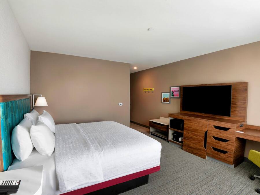 Quarto de hotel com cama, escrivaninha, televisão e cadeira.