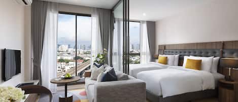 Quarto de hotel moderno com uma cama grande, um sofá, uma mesinha e uma TV.