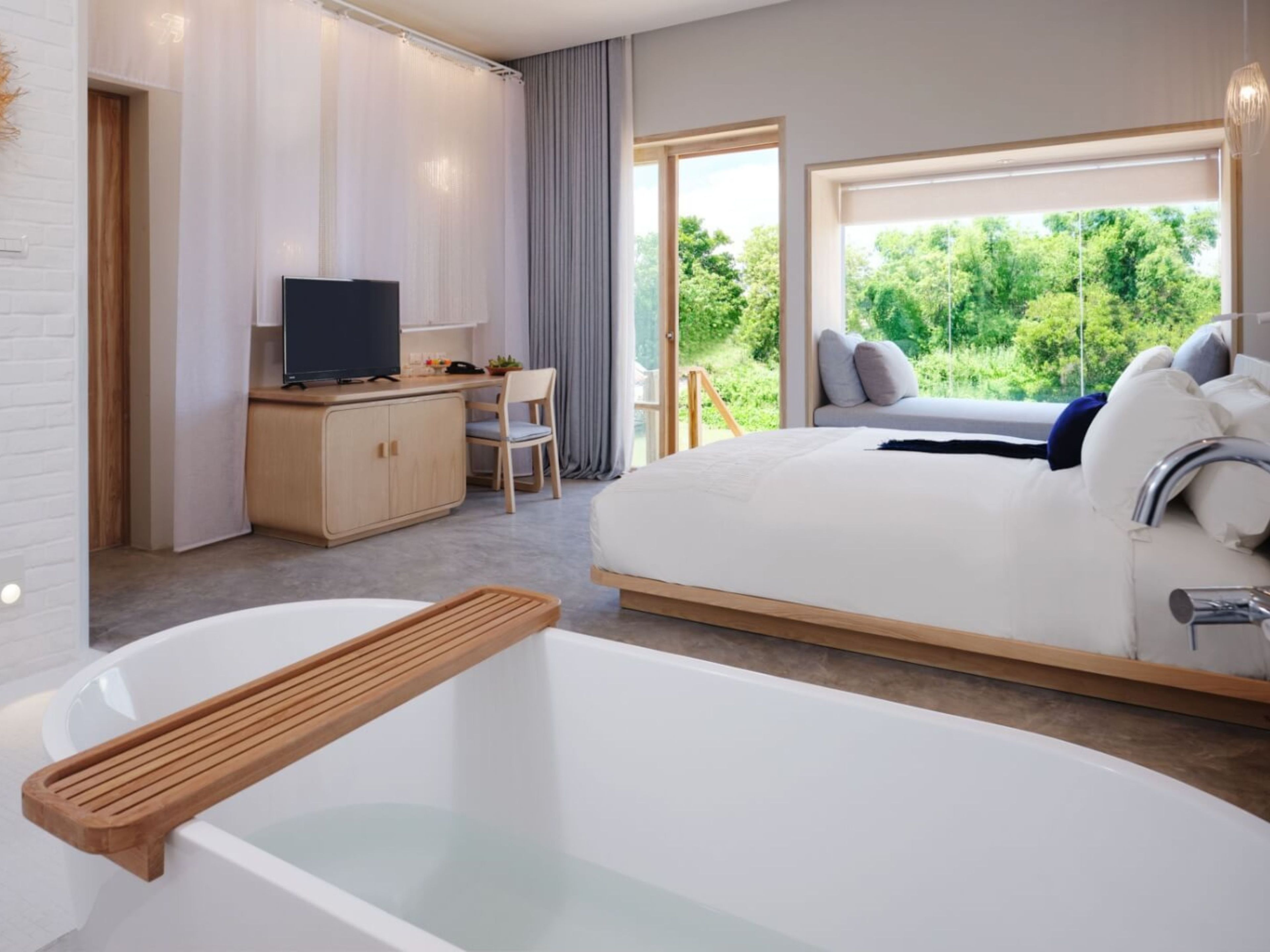 Quarto moderno com uma cama grande, televisão, escrivaninha e banheira.