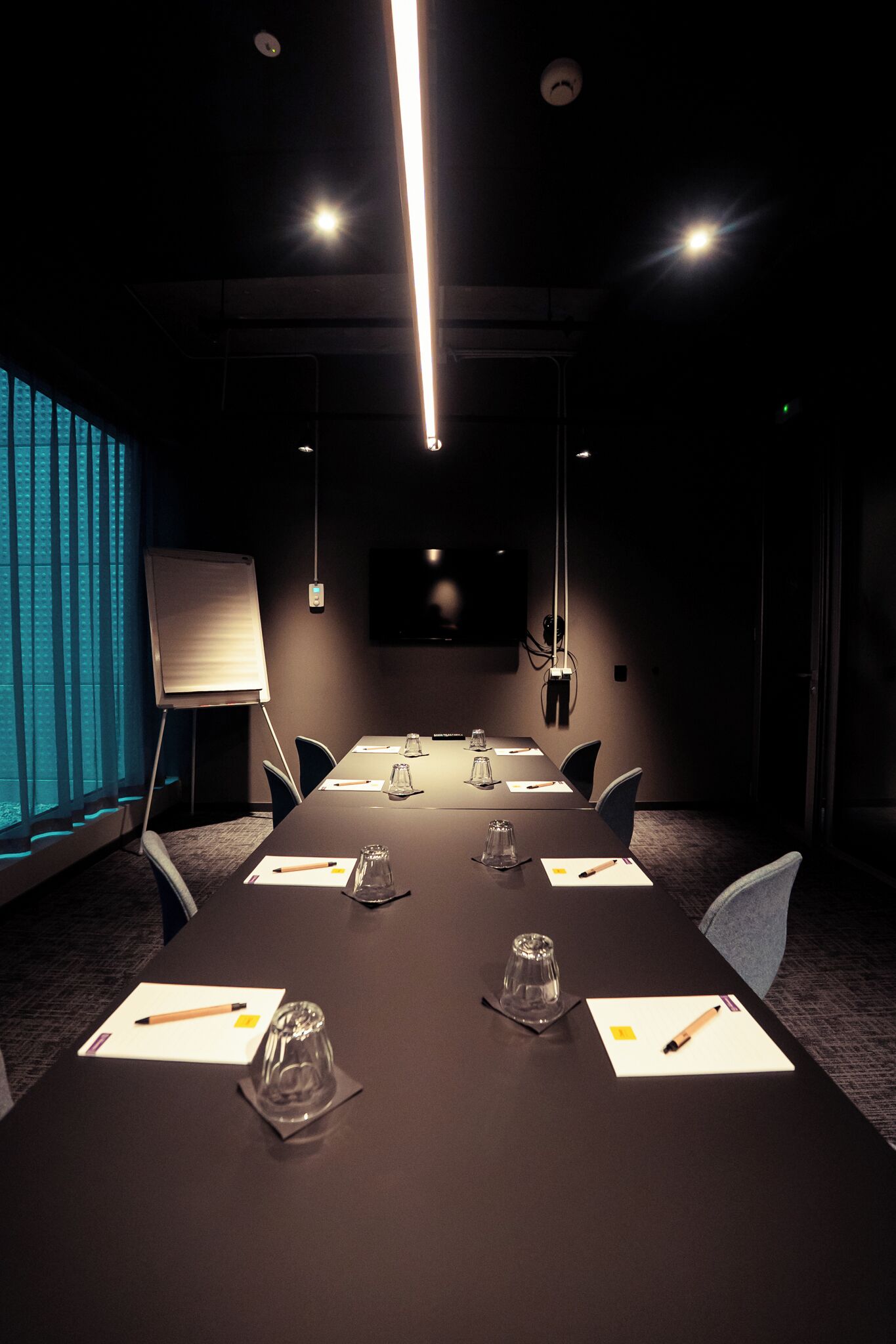 Uma sala de conferências com uma mesa comprida, cadeiras, um quadro branco e uma tela de projetor.