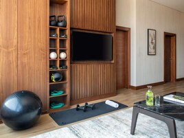 Quarto com aparador de madeira contendo equipamentos de ginástica, uma bola de exercícios preta grande, um tapete de exercícios preto e uma mesa de mármore com um livro e uma garrafa.