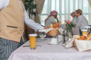 Mesa posta para quatro pessoas, com pão, doces e um vaso de flores.
