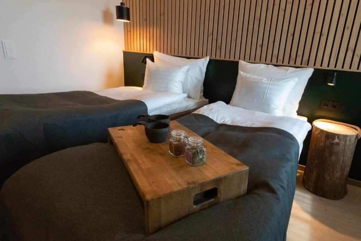 Quarto com duas camas, uma mesa de cabeceira de madeira e uma pequena mesa com frascos.