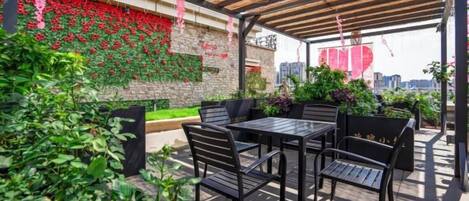 Um pátio externo com mesa e cadeiras, cercado por vegetação e vista para a cidade.