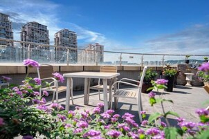 Terraço no telhado com mesa e cadeiras, rodeado por vasos de plantas e flores.