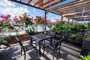 Um pátio externo com mesa e cadeiras, rodeado por vasos de plantas e flores.