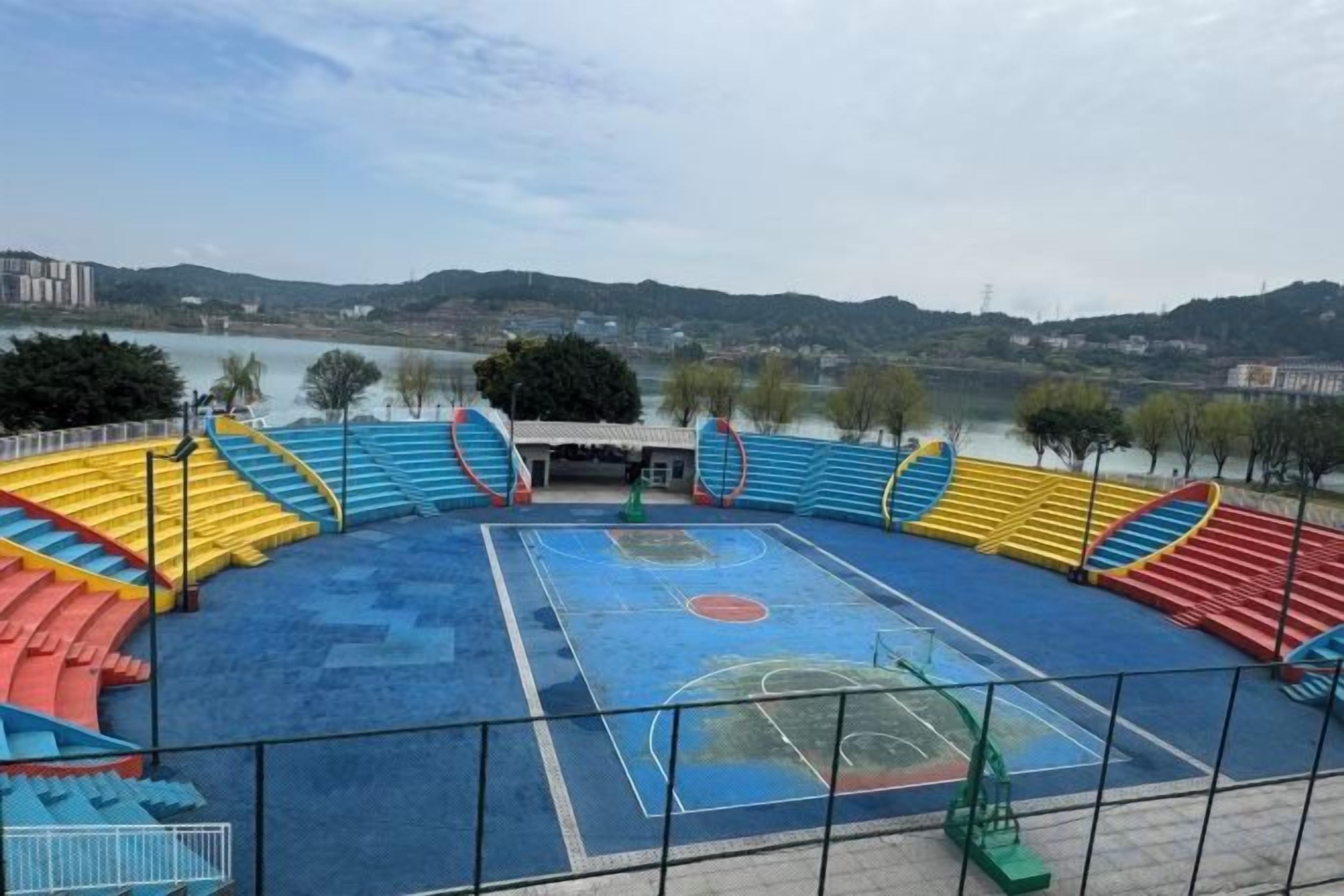 Quadra de basquete ao ar livre com vista para um corpo d'água e colinas ao fundo.
