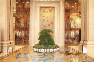 Um saguão com planta central, piso estampado e parede decorativa.