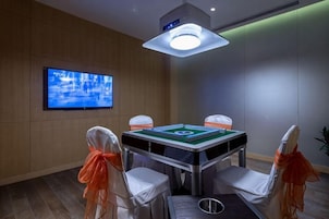 Quarto com mesa de bilhar, quatro cadeiras com fitas laranja, televisão na parede e luminária no teto.