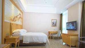 Quarto de hotel com cama, escrivaninha, cadeira, televisão e cômoda.