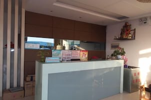 Balcão de recepção com divisória de vidro, planta e cartazes informativos.