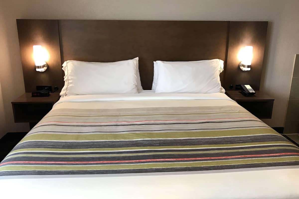 Quarto de hotel com uma cama grande, duas mesas de cabeceira e luminárias fixadas na parede.