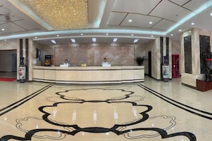 Uma área de recepção de hotel com piso de mármore, balcão de recepção e um grande candelabro.